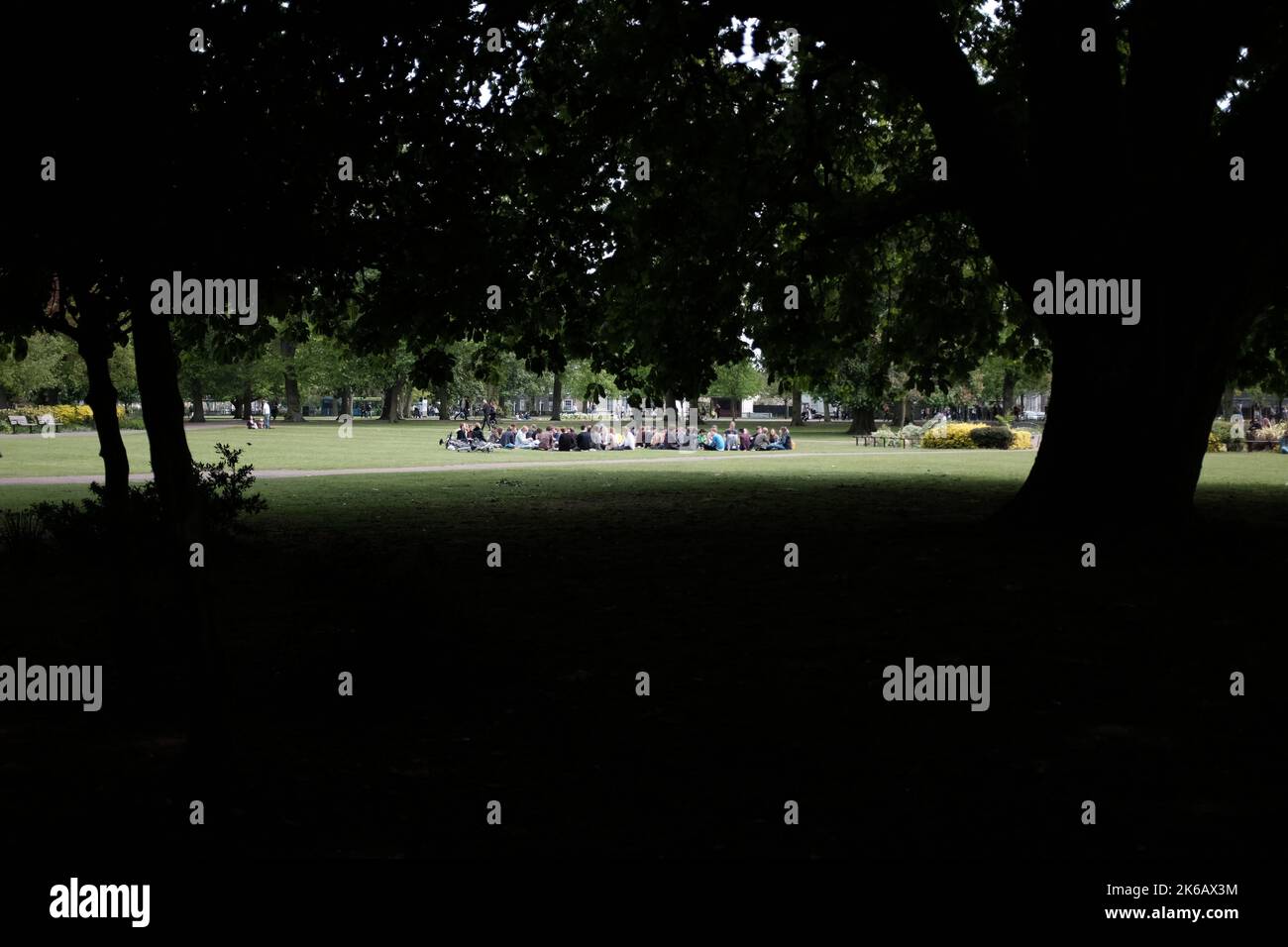 A large group of people sat in a circle in Victoria Park seen behind ...