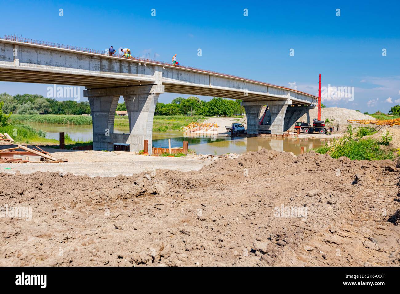 Team of workers are working on the unfinished bridge, road over river ...