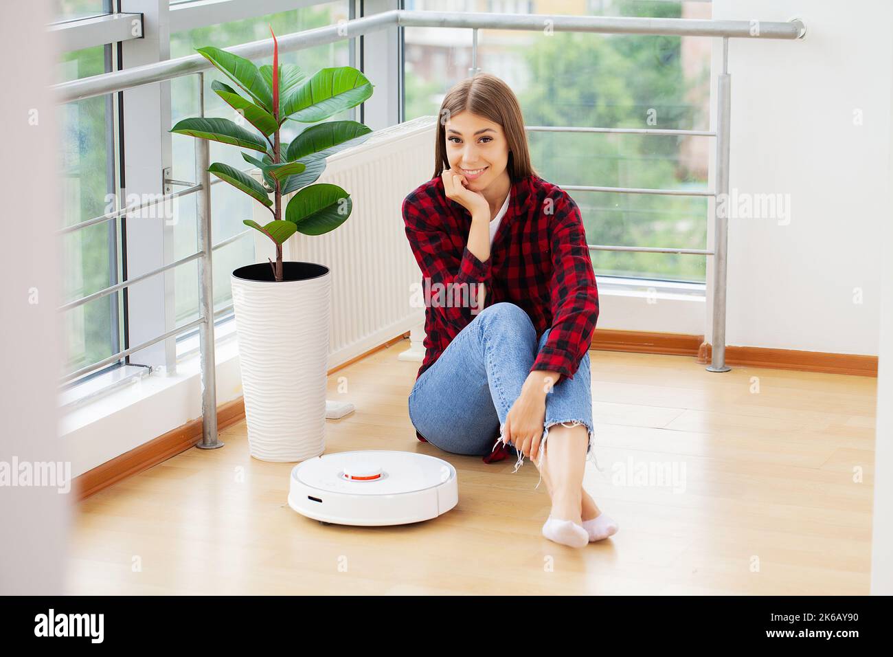 White robotic vacuum cleaner cleaning the floor while woman sitting ...