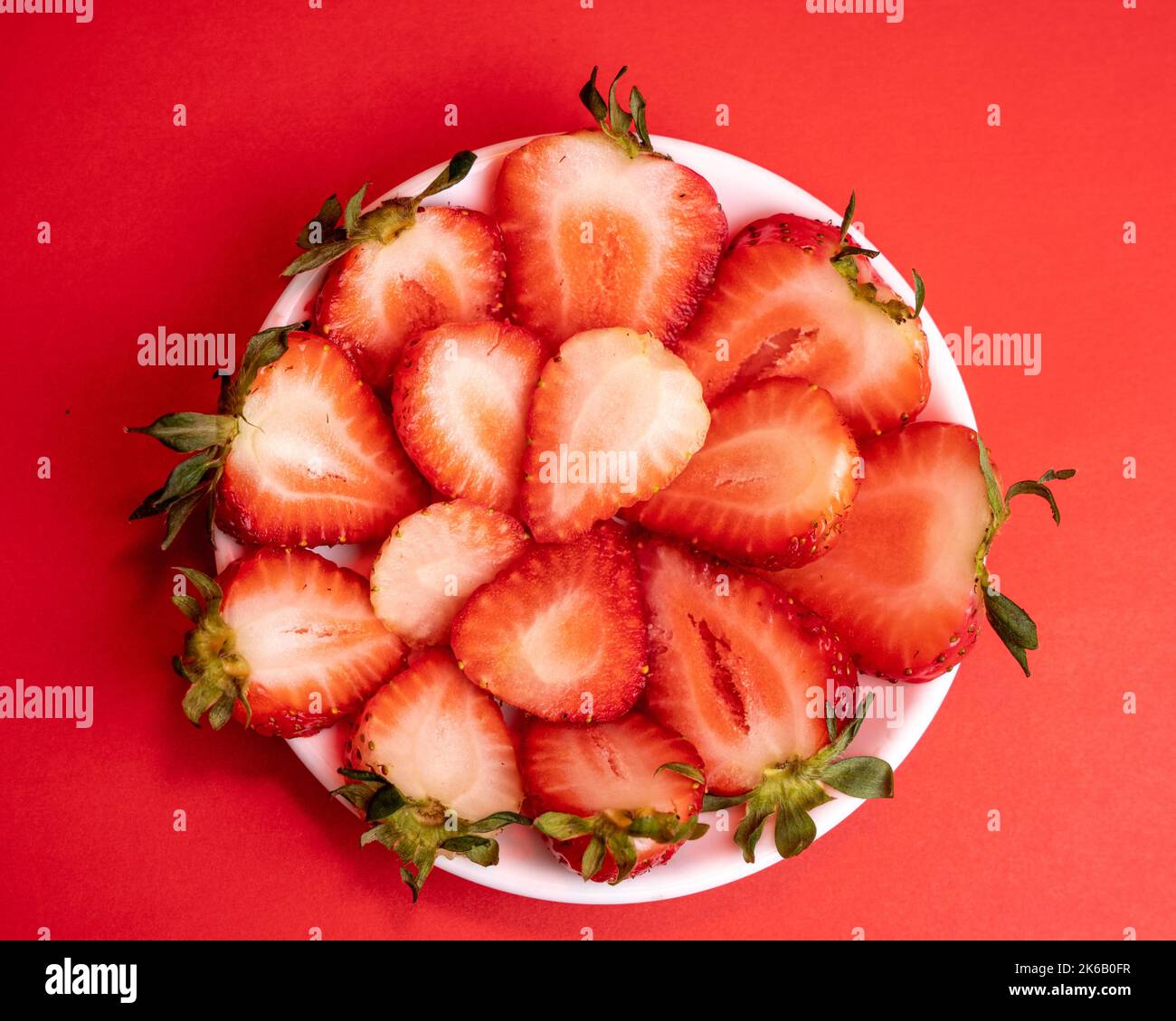 A top view of a bowl of halved and sliced strawberries on a red ...