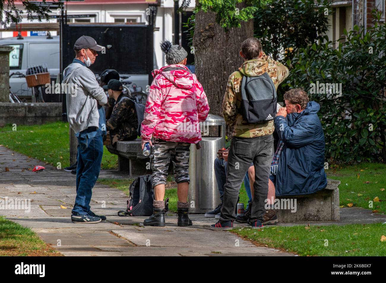 group of alcoholics standing together in the park drinking cans of ...