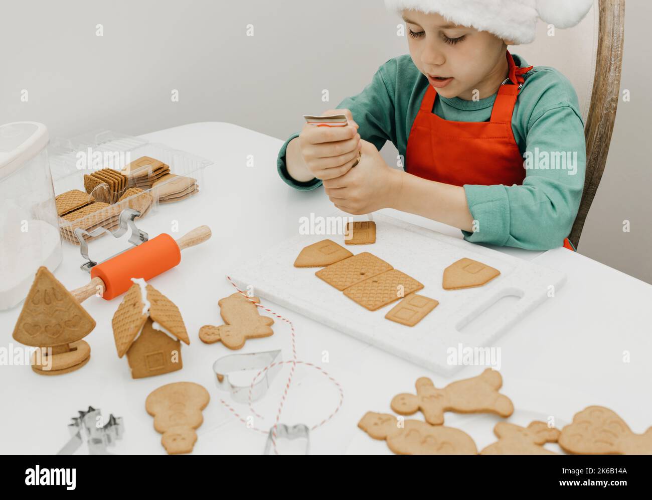 A cute boy decorates gingerbread cookies in Santa's hat on New Year's ...