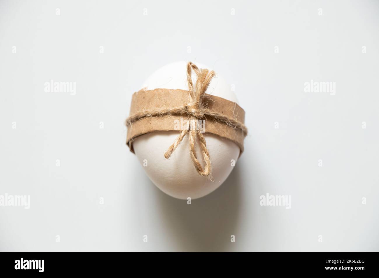 One white chicken egg tied with a rope lies on a white background ...