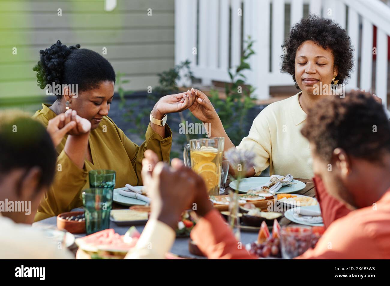 Big African American family saying grace at table outdoors and holding ...