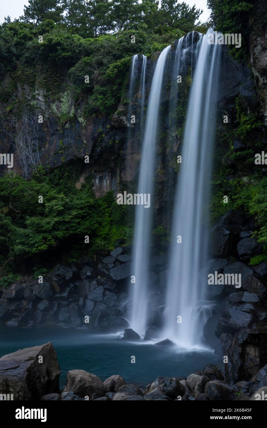A vertical shot of the splashing flowing Jeongbang waterfall in Jeju ...