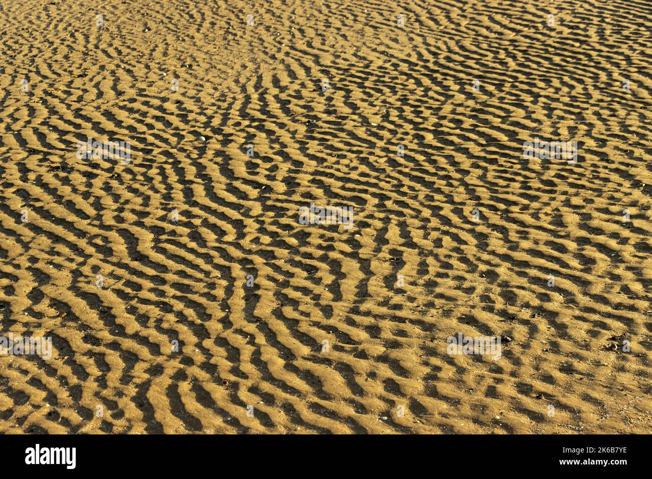 The receeding waters on a tidal sandy beach has left a pattern of ...