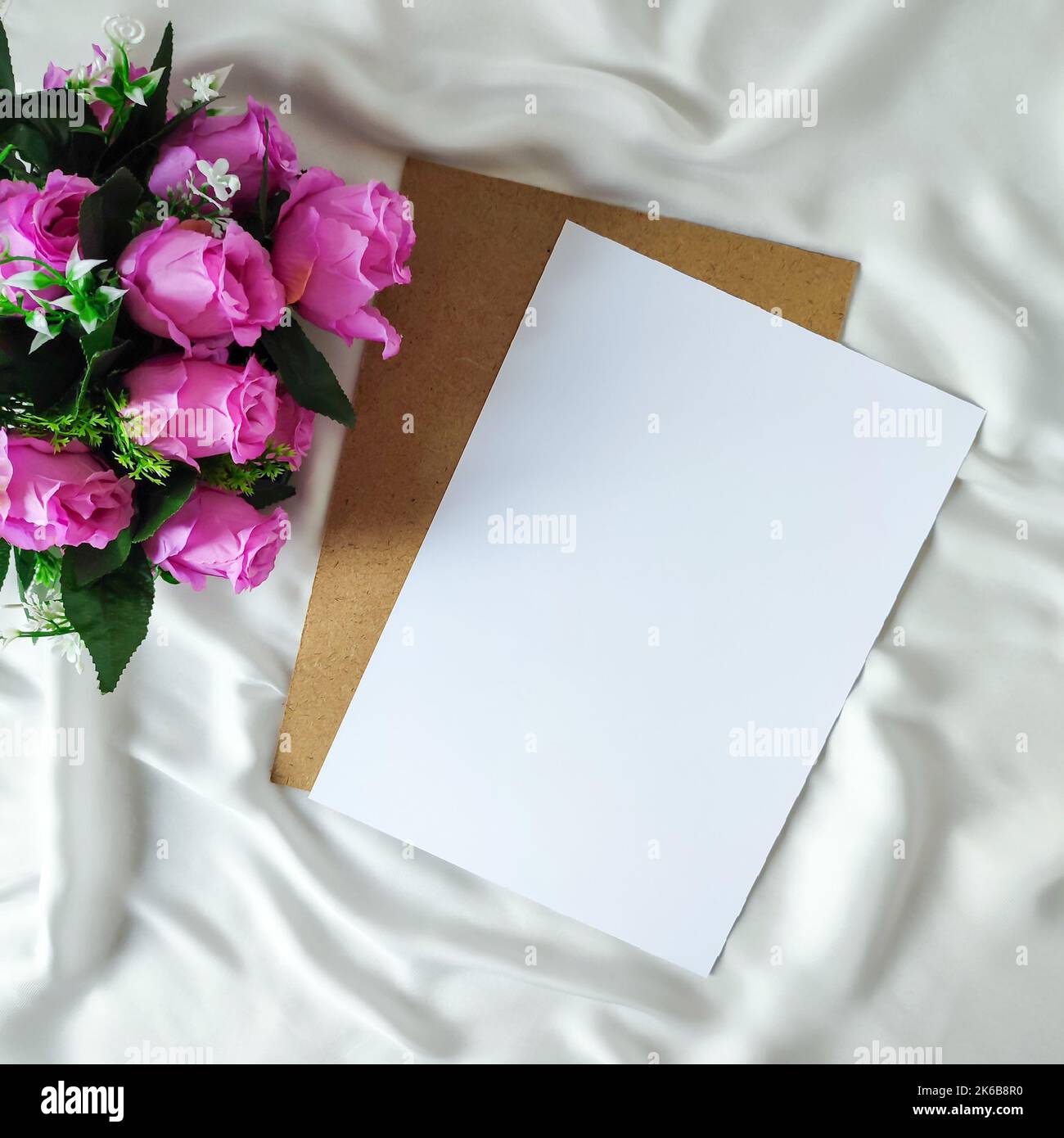 A bunch of artificial purple roses and blank paper on the white piece ...