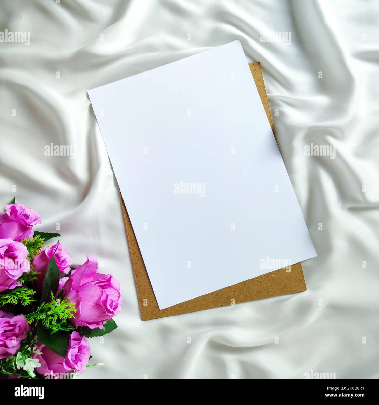 A top view of blank piece of paper and artificial flowers on the white ...