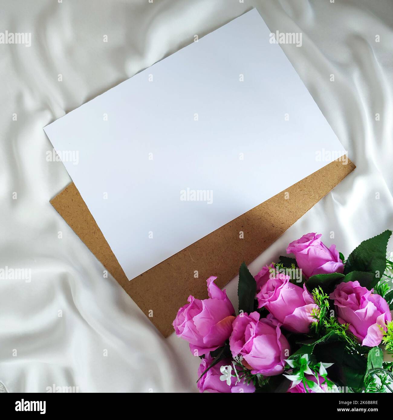 A top view of artificial bouquet and blank paper on the white piece of ...