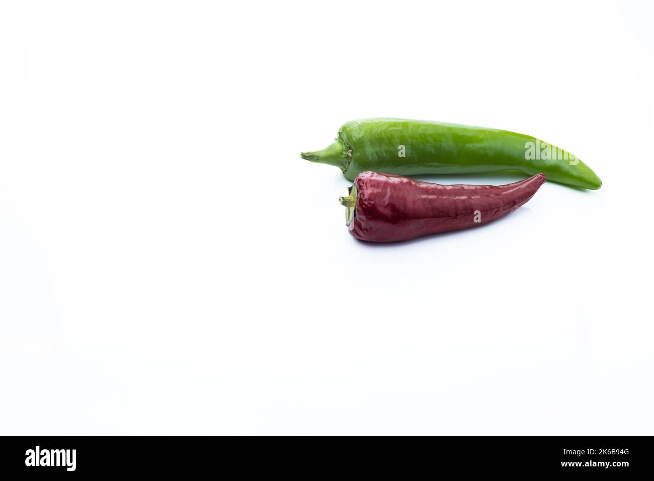 A green chili pepper and a dark red chili pepper isolated on a white ...
