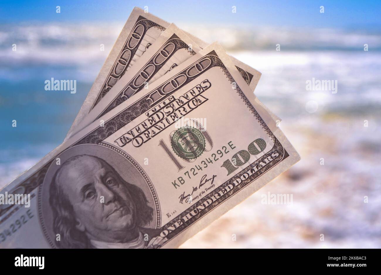 Girl holding money bill of 300 dollars on background of sea ocean waves and blue sky close-up ...