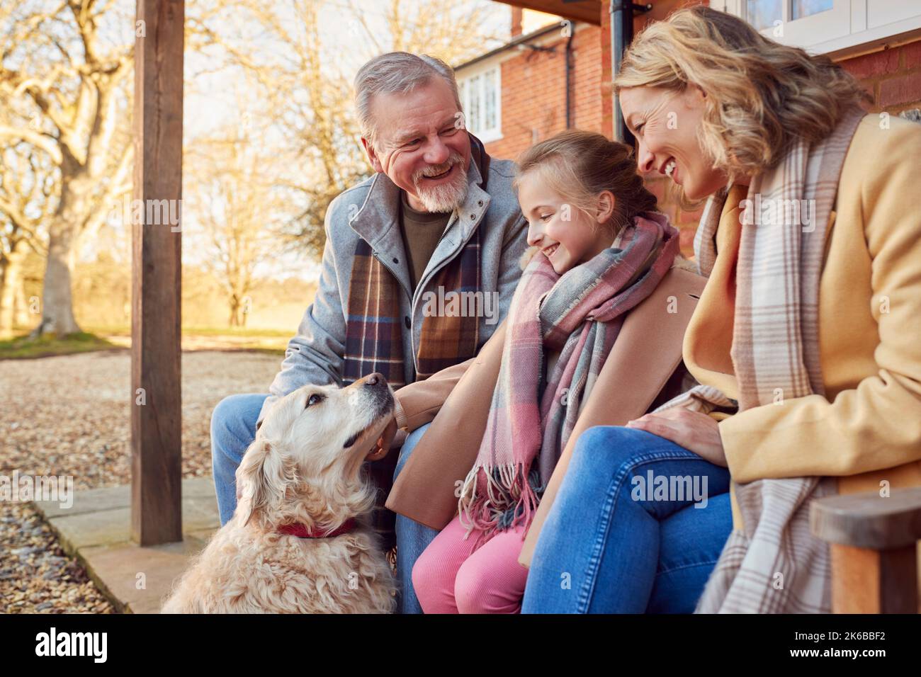 Grandparents With Granddaughter And Pet Dog Outside House Getting Ready To Go For Winter Walk ...