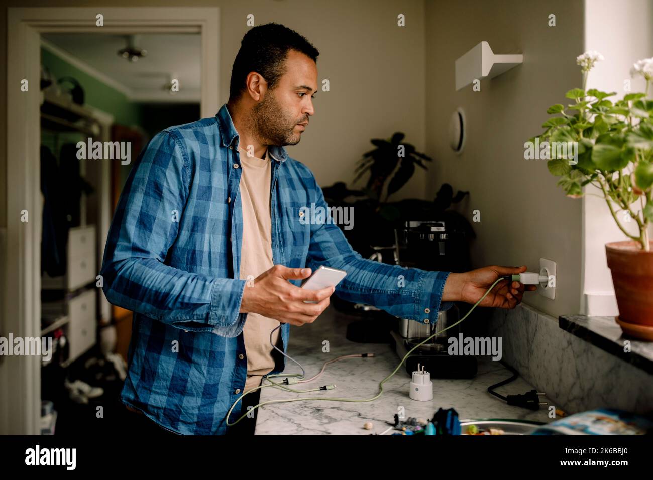 Man plugging smart phone charger in power socket while standing near ...