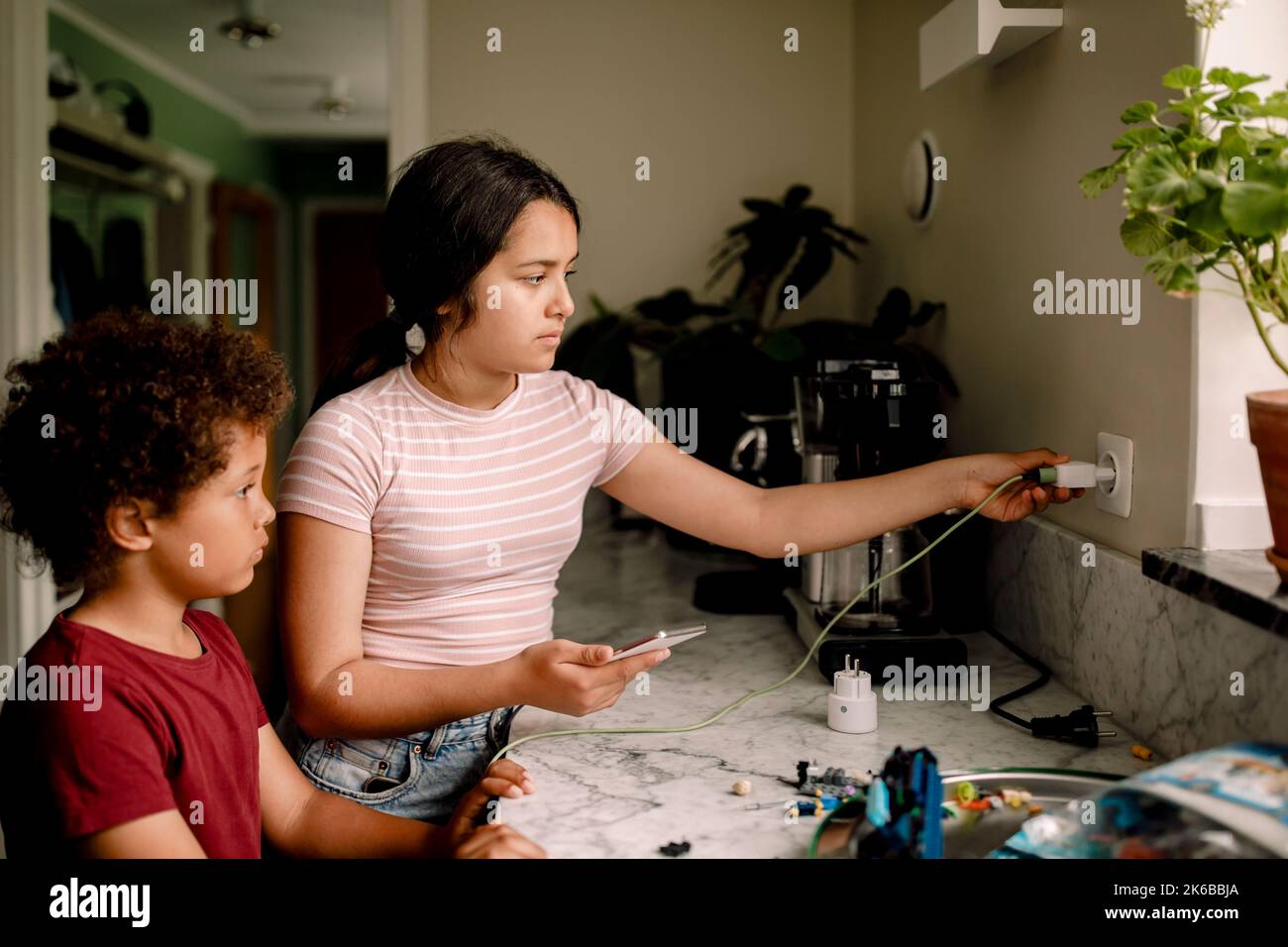 Girl charging smart phone while standing with brother near kitchen ...