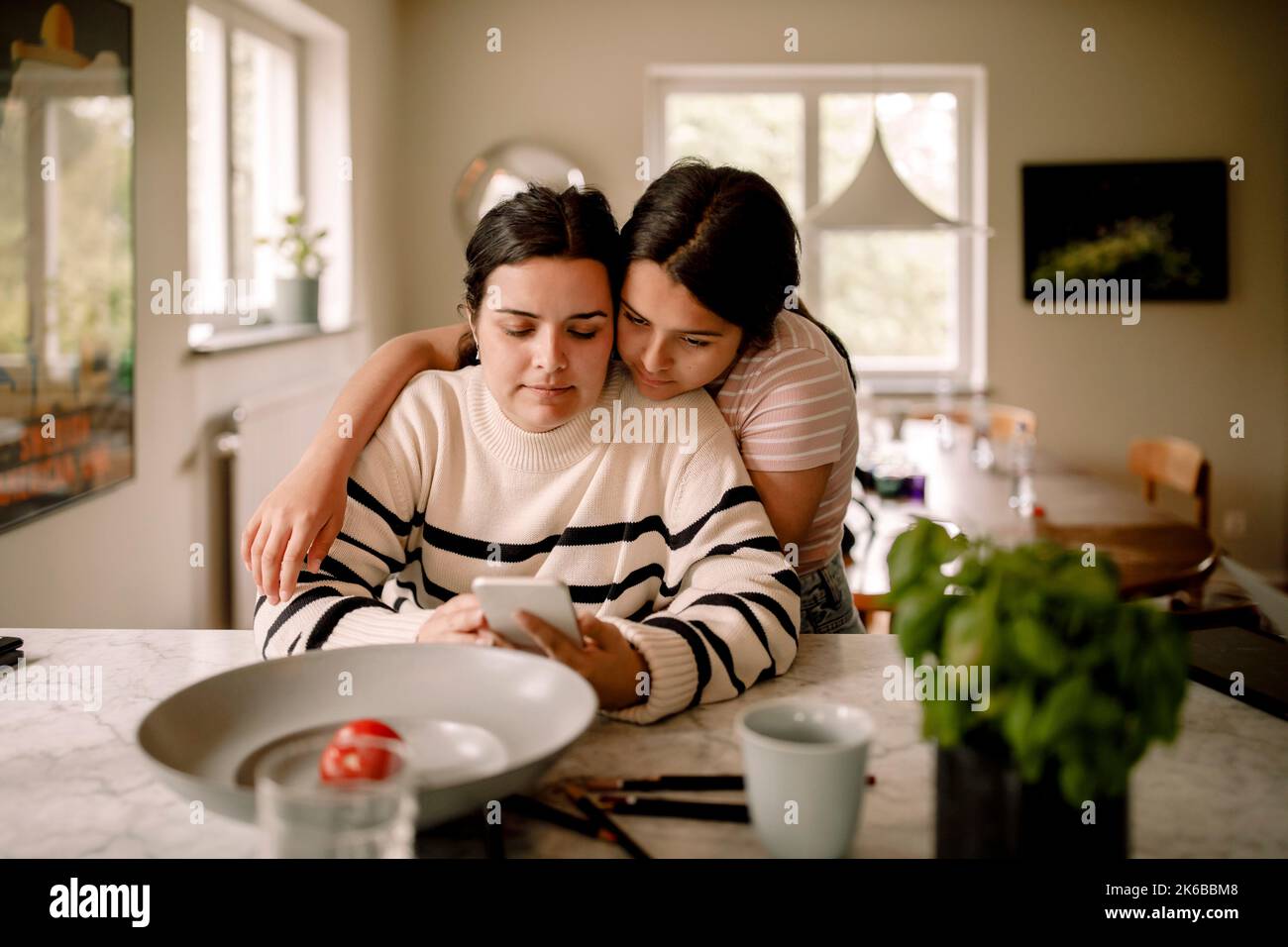 Daughter with arm around mother using smart phone at home Stock Photo ...