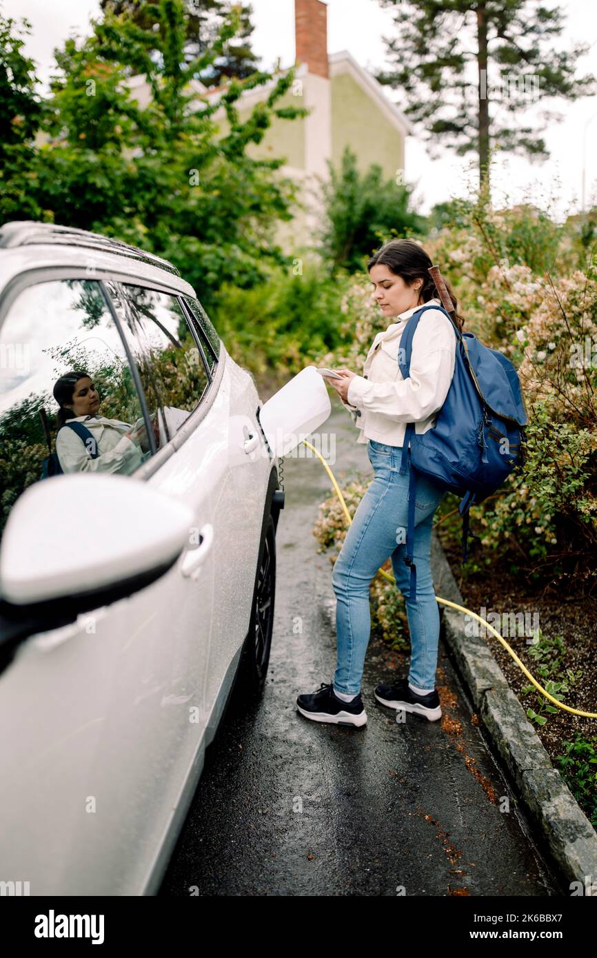 Side view of woman using smart phone while charging electric car Stock ...