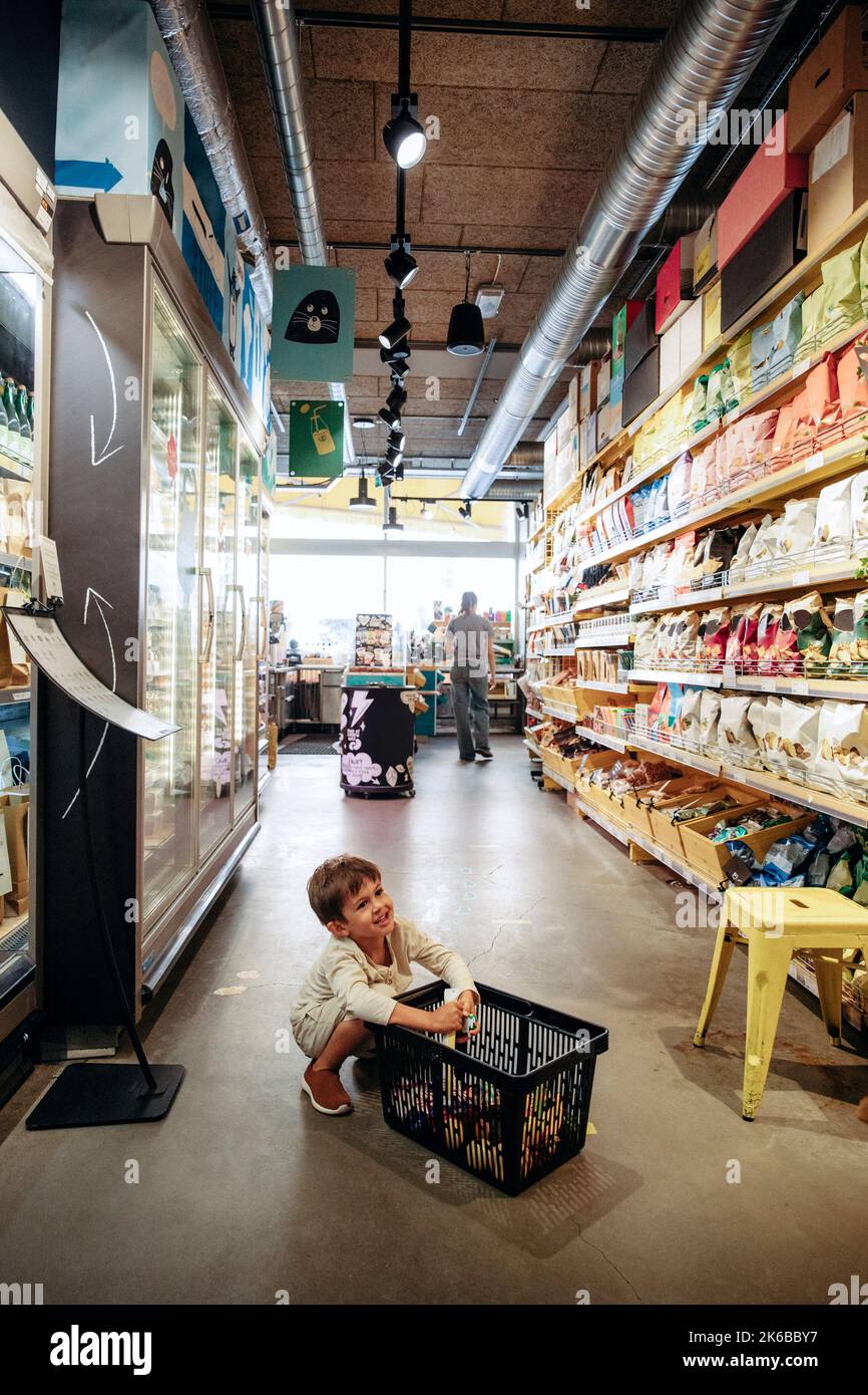 Boy with shopping basket crouching at aisle in supermarket Stock Photo ...