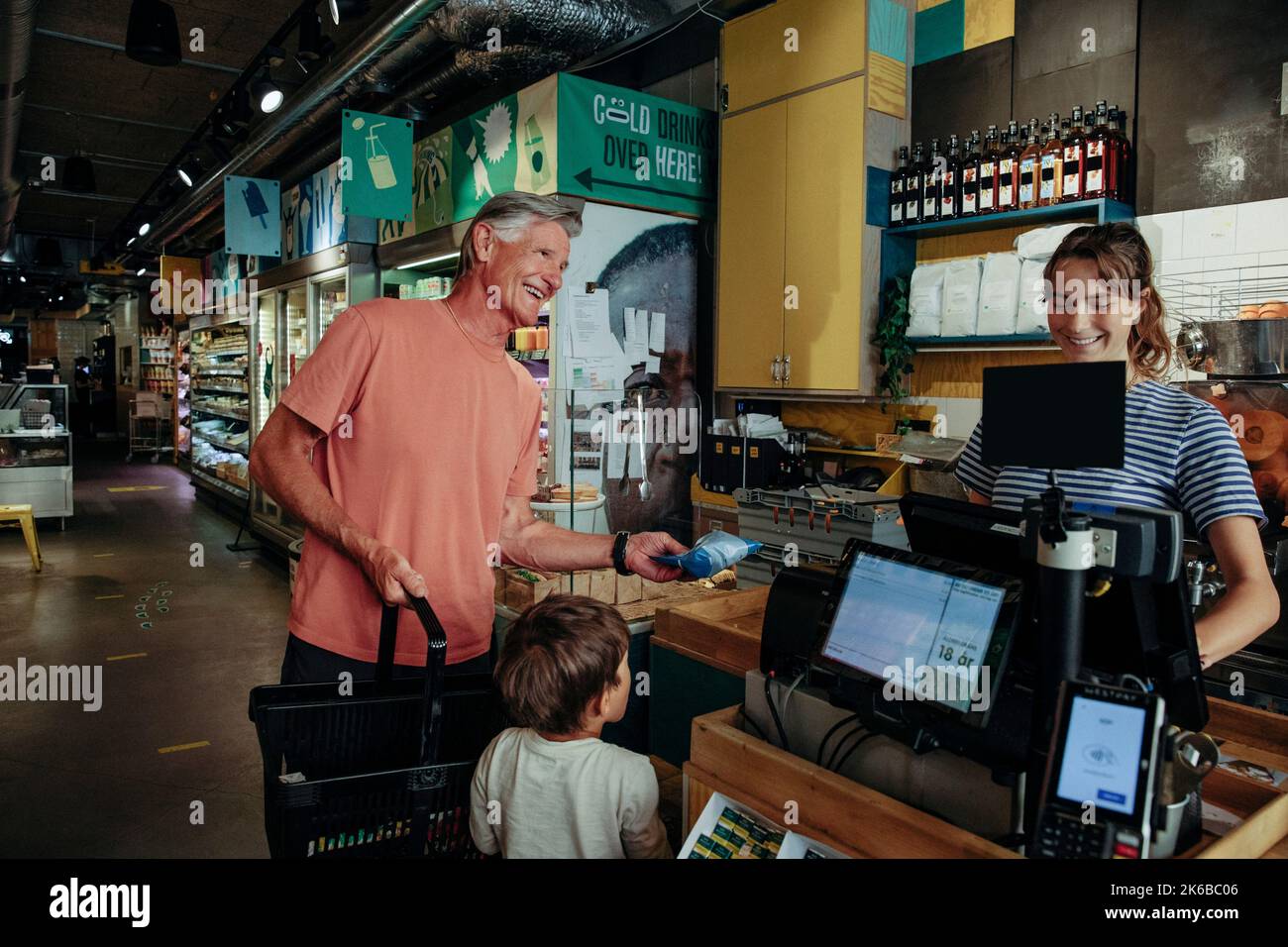 Happy senior man talking to cashier while standing with grandson at ...