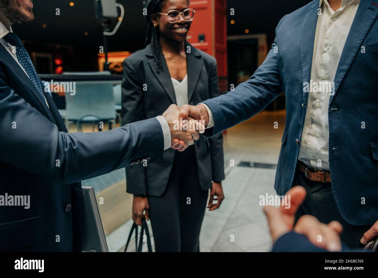 Businessmen handshaking by female colleague in hotel lounge Stock Photo ...