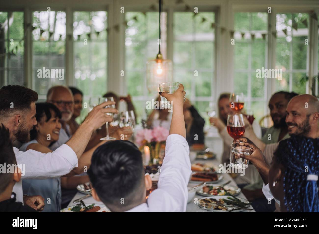 Multi-generation family toasting drinks during dinner party at home ...