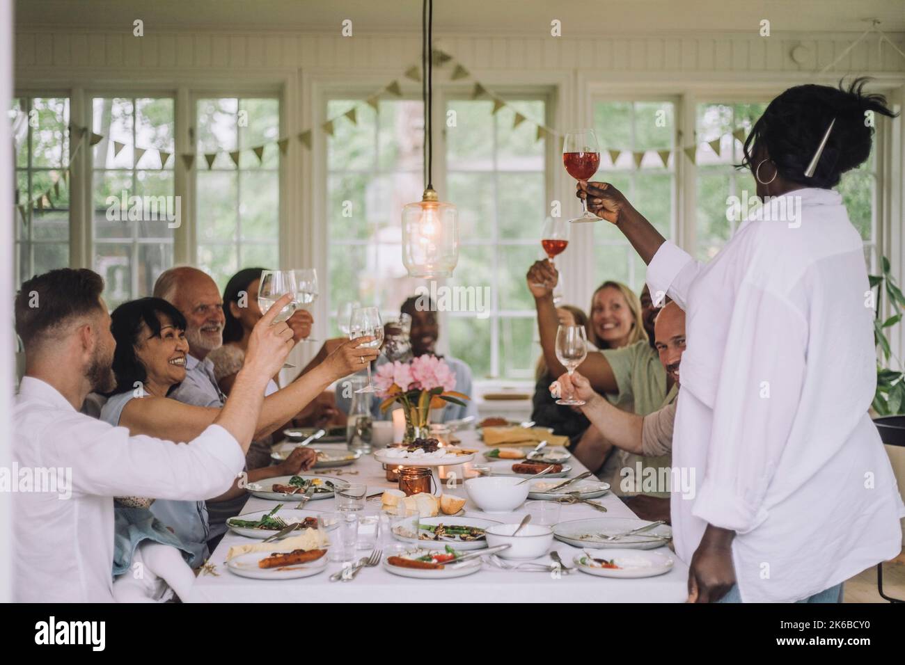 Woman toasting drinks with multi-generation family at dining table ...