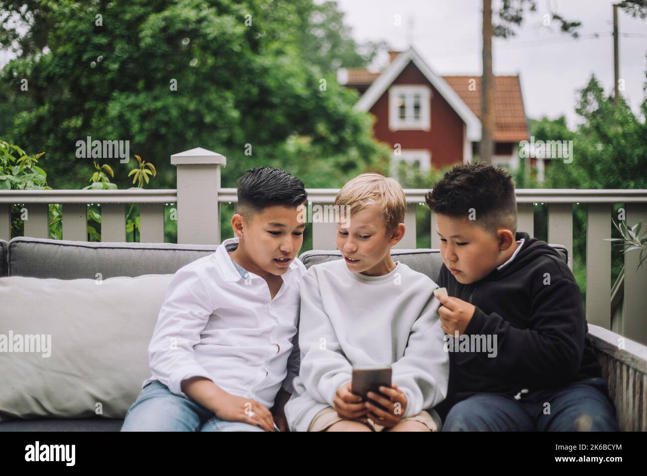 Excited boys sharing smart phone while sitting together on couch Stock ...