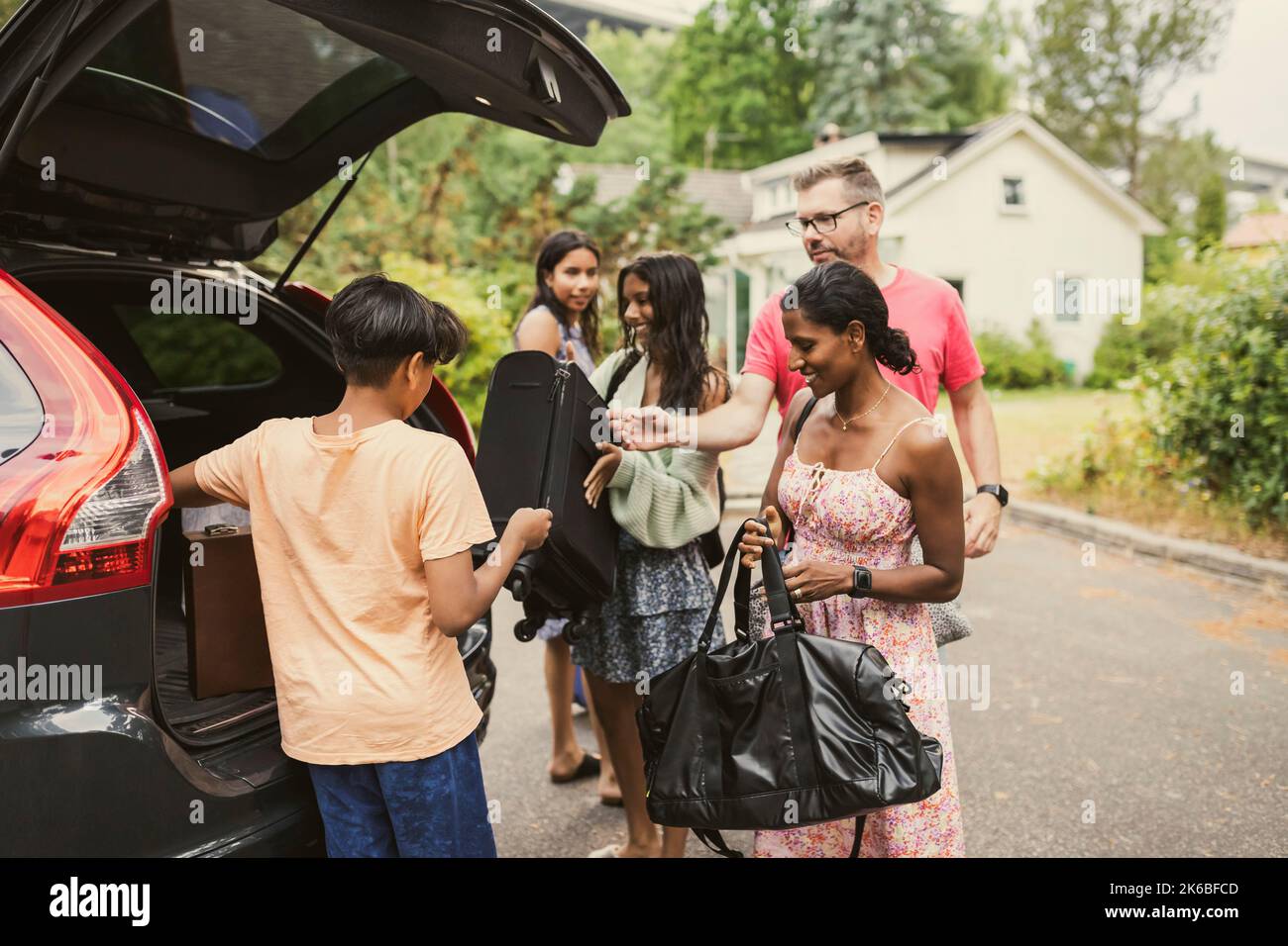 Multiracial family unloading luggage from car trunk while standing on ...