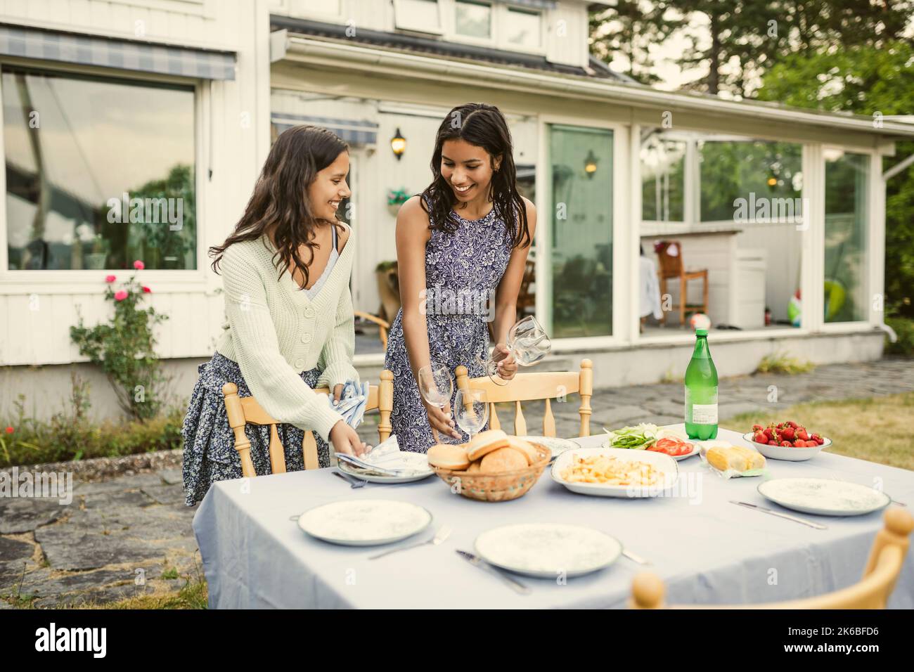 Smiling sisters setting up table at back yard Stock Photo - Alamy