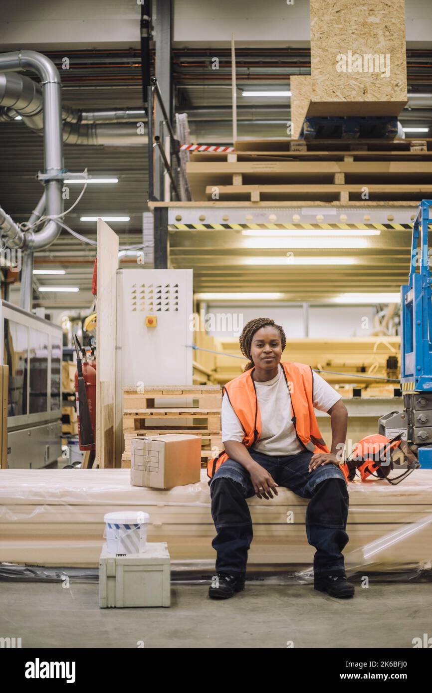 Portrait of female blue-collar worker sitting by hardhat in warehouse ...
