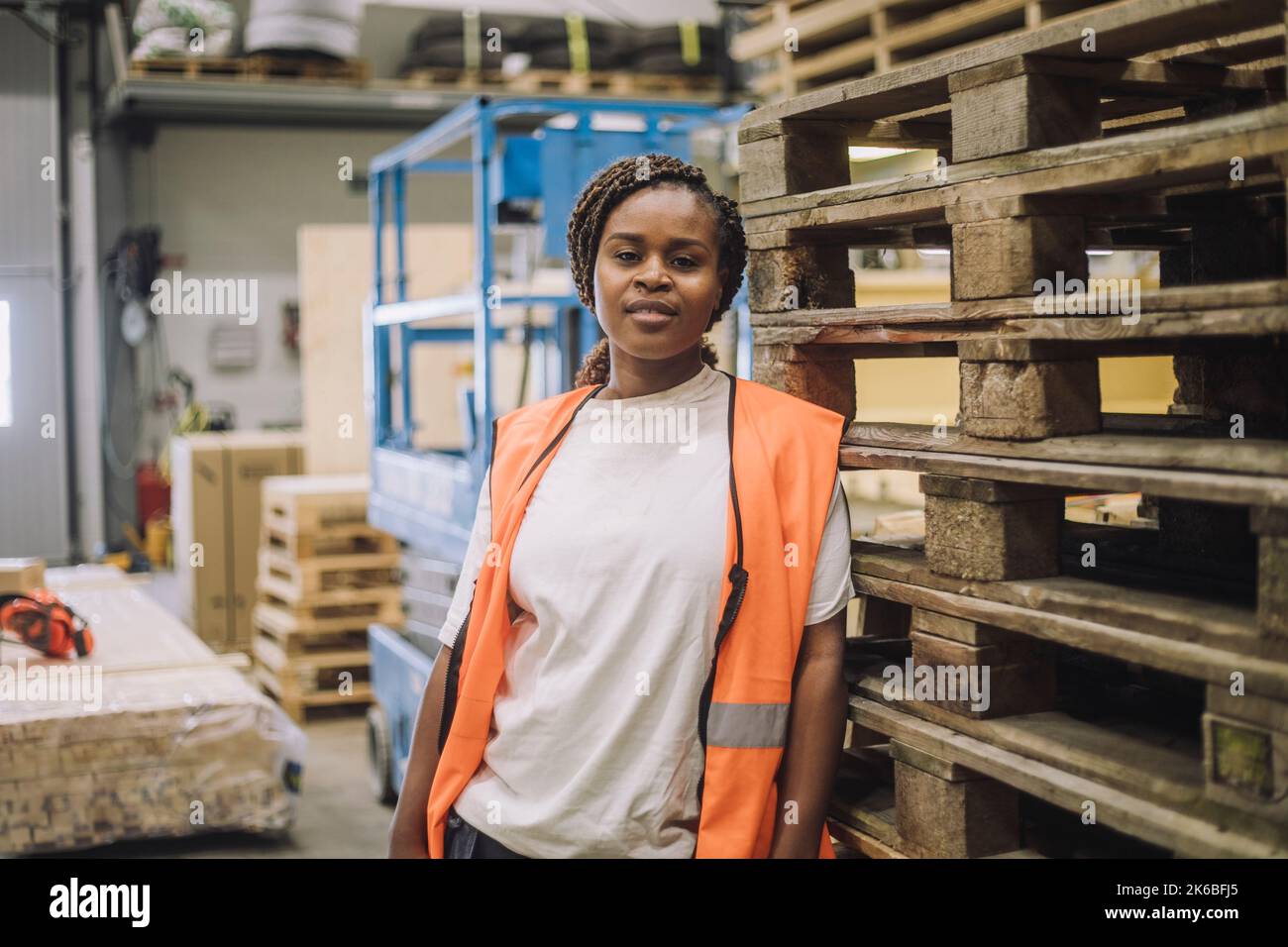 Portrait of female carpenter leaning on pallet stack in warehouse Stock ...