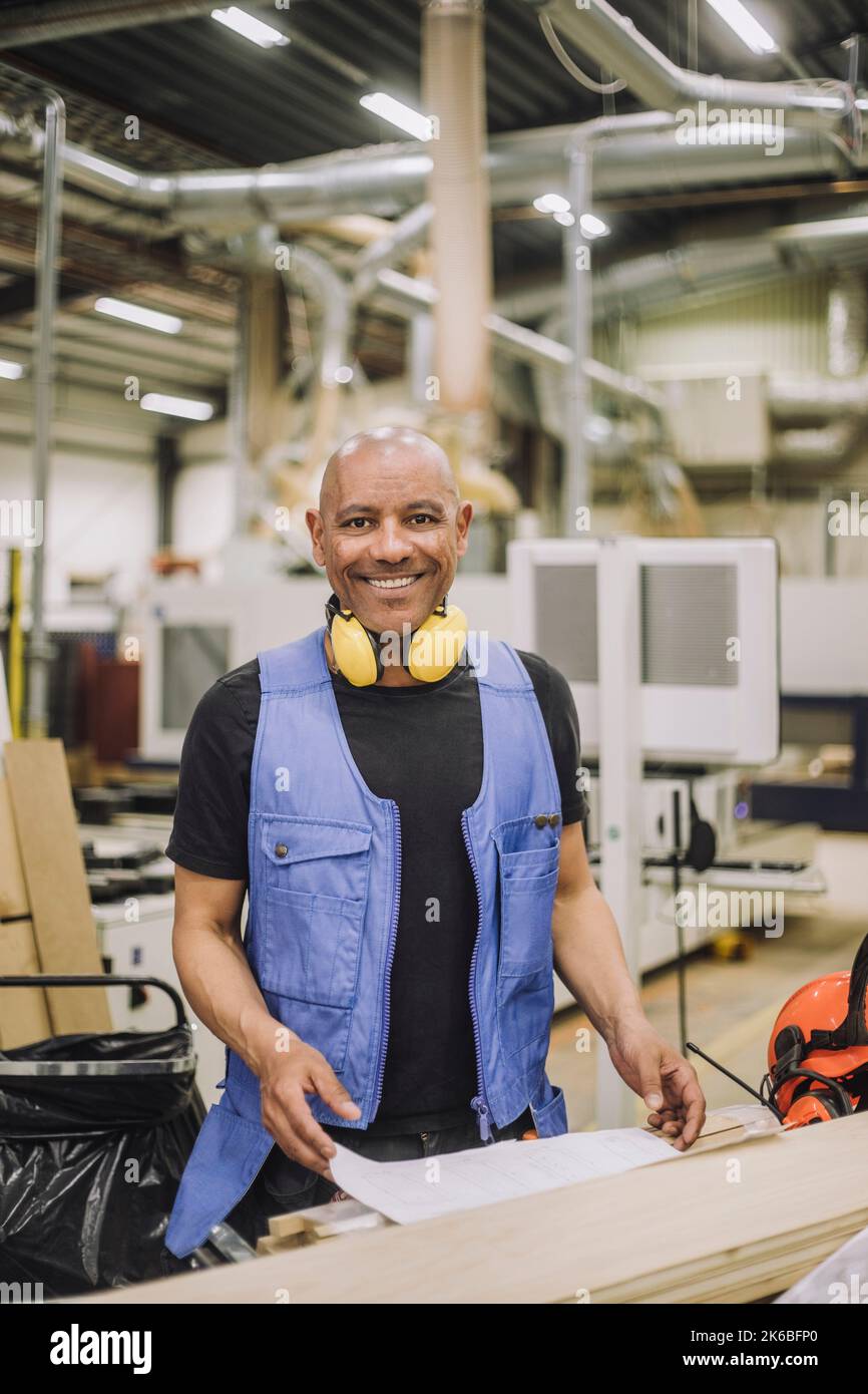 Portrait of smiling carpenter with ear protectors working in warehouse ...