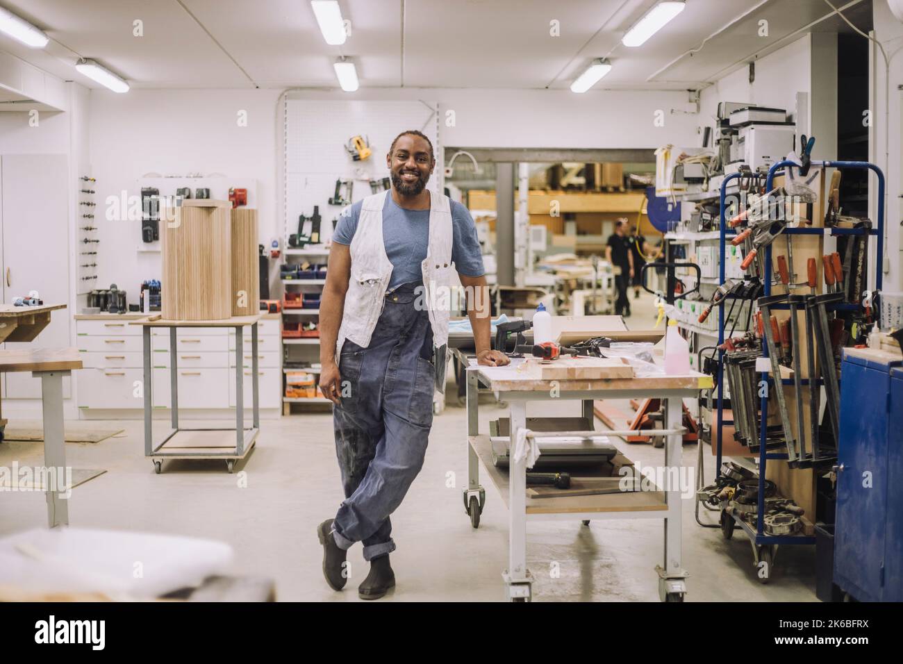 Full length portrait of smiling carpenter standing on one leg while ...