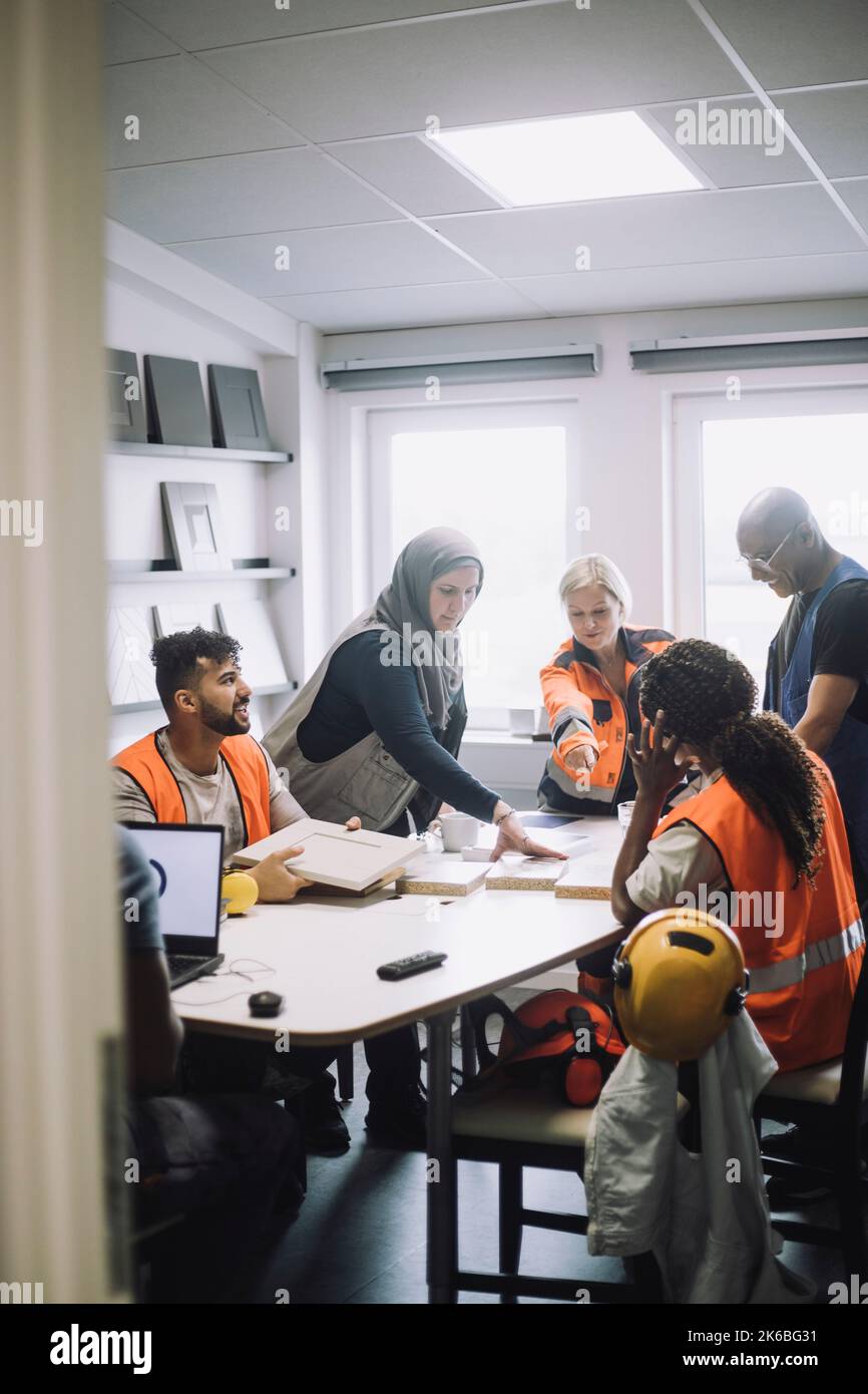 Female carpenter discussing over wooden block with colleagues at desk ...