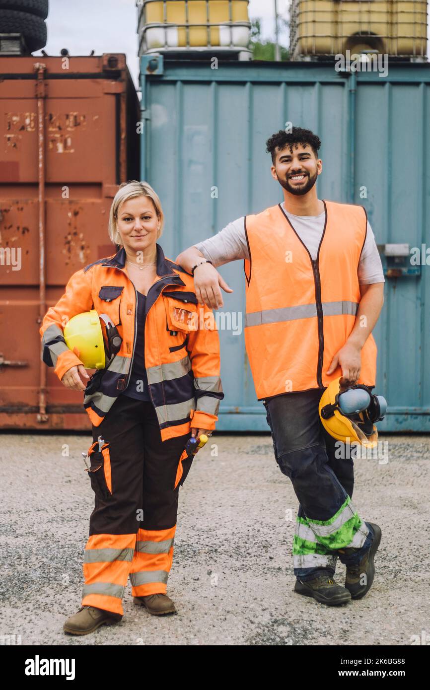 Full length of smile male and female construction workers in reflective clothing standing at ...
