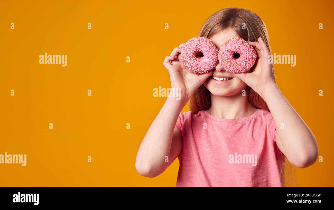 Studio Portrait Of Girl Holding Two Donuts In Front Of Eyes Against ...