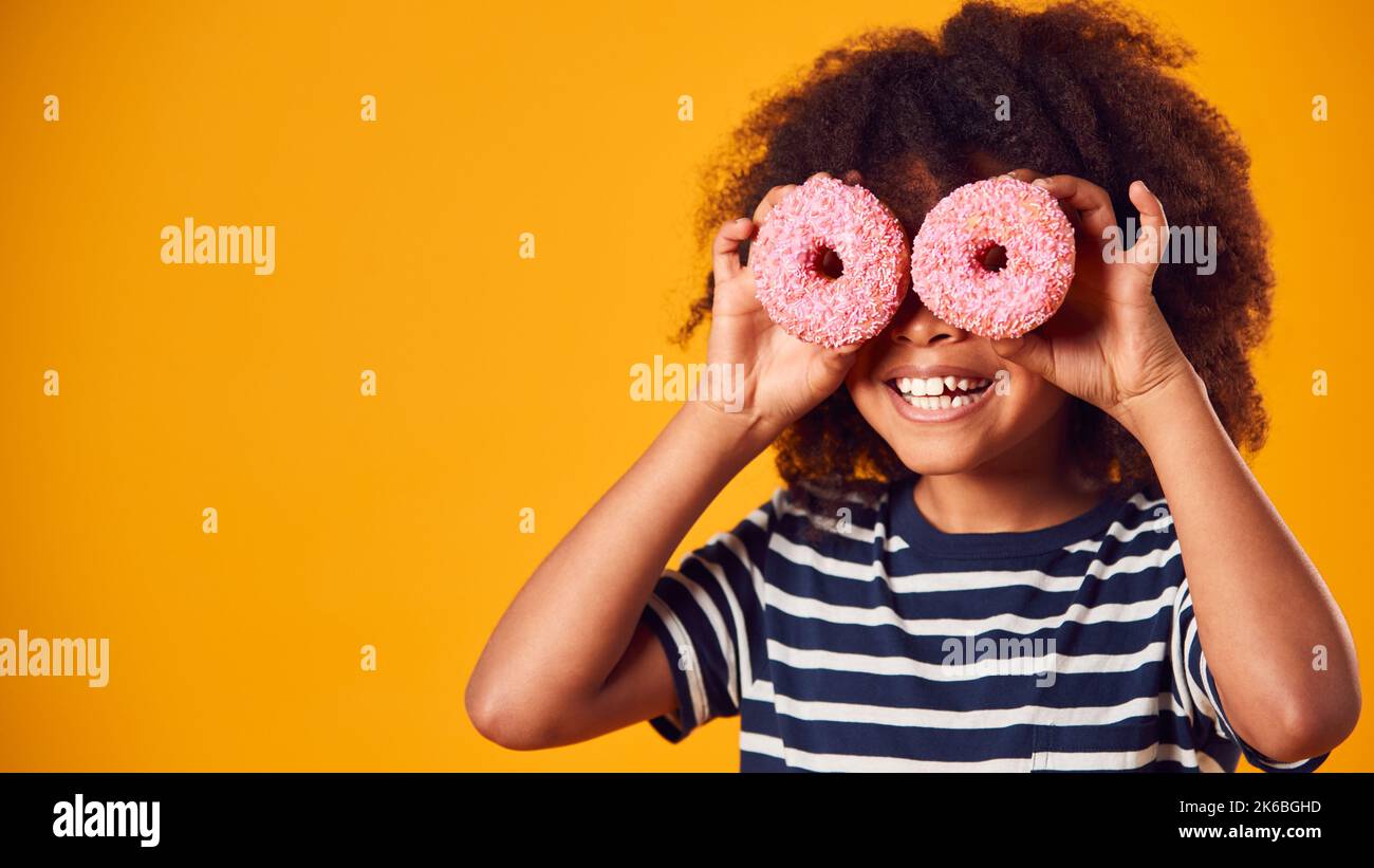 Studio Portrait Of Boy Holding Two Donuts In Front Of Eyes Against ...