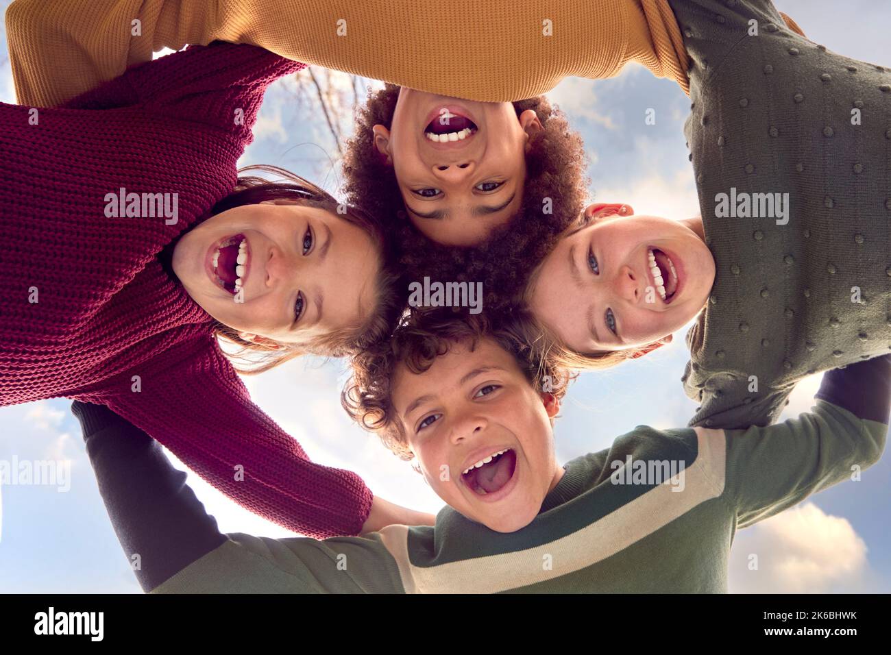 Low Angle Portrait Of Children Having Fun Playing Outdoors Linking Arms Looking Down Into Camera ...