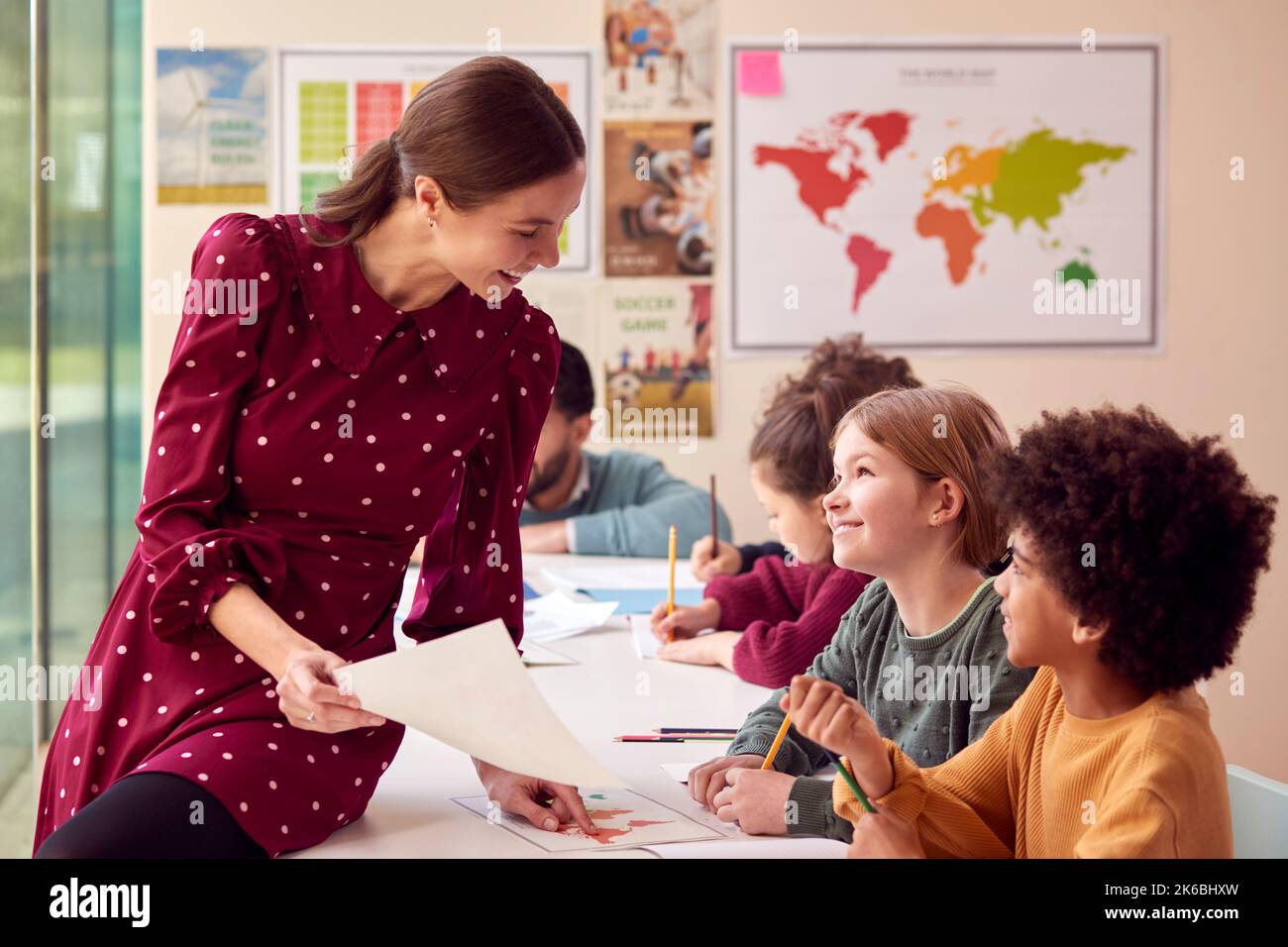 Smiling Female Elementary School Teacher Working At Desk In Classroom ...