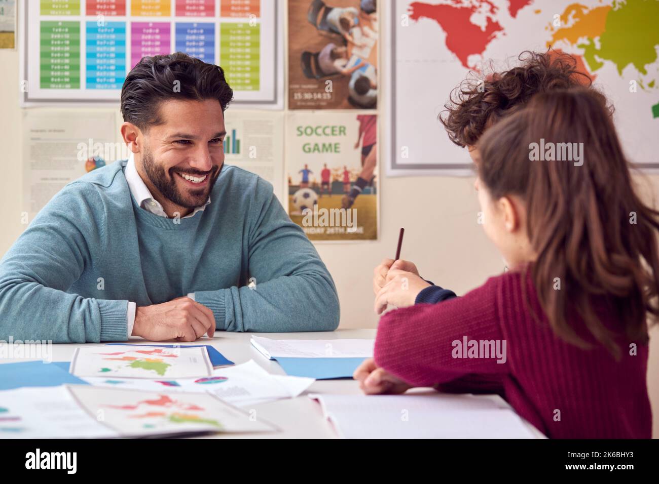 Smiling Male Elementary School Teacher Working At Desk In Classroom ...