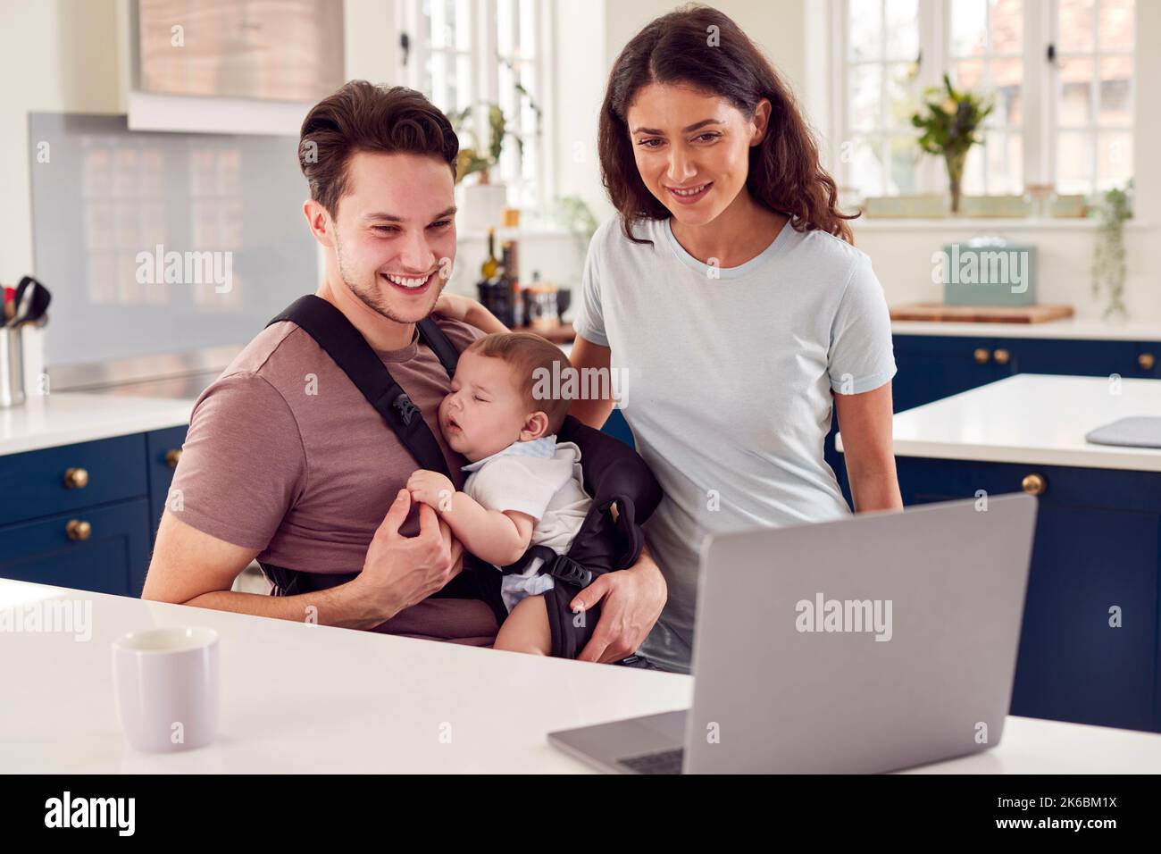 Transgender Family With Baby Working From Home Looking At Laptop On ...