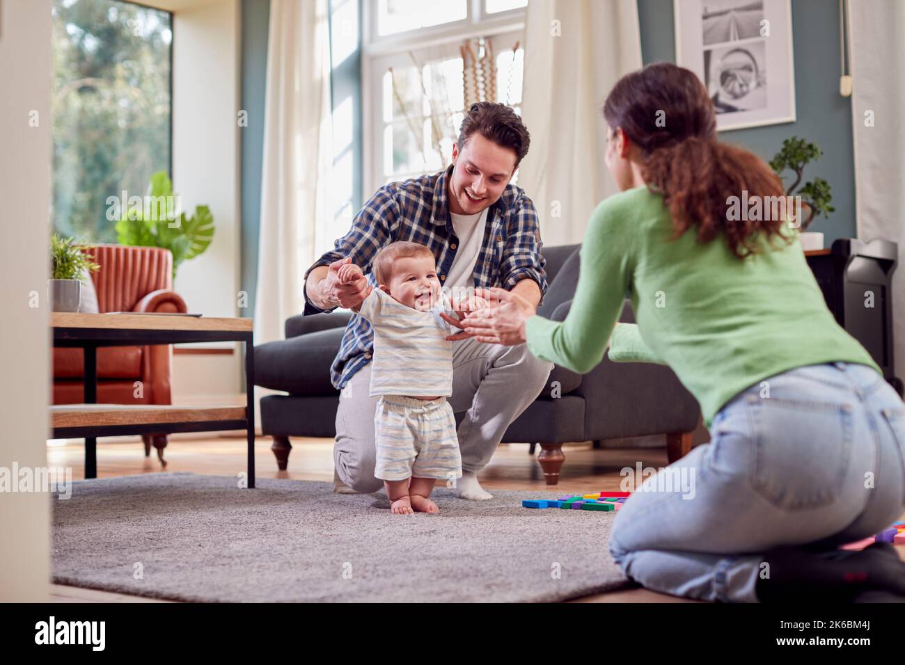 Transgender Family Encouraging Baby To Take First Steps In Lounge At ...