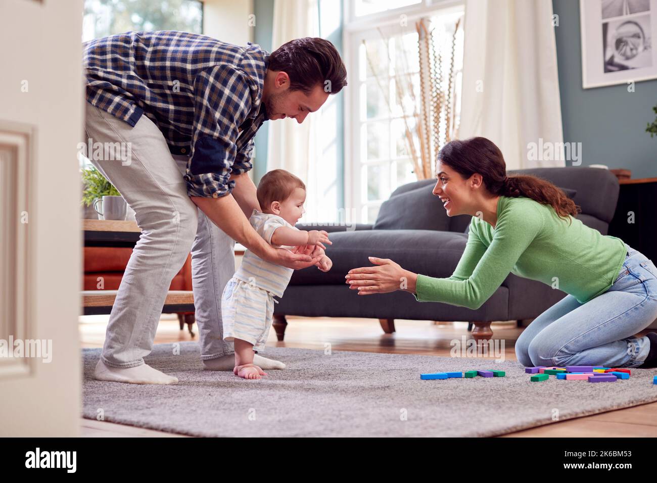 Transgender Family Encouraging Baby To Take First Steps In Lounge At ...