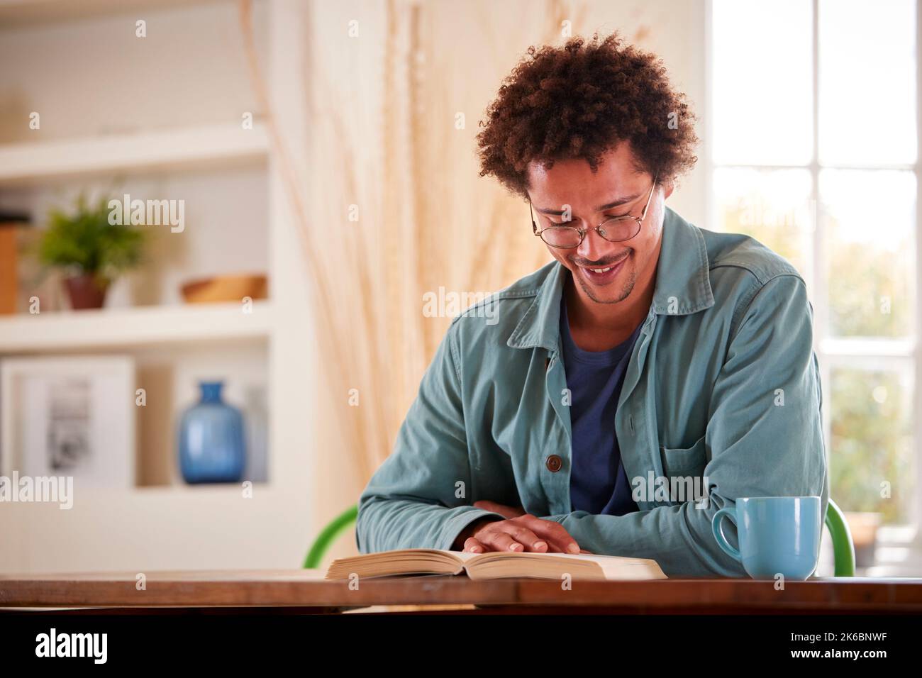 Man Relaxing At Home Sitting At Table Reading Book With Hot Drink Stock ...