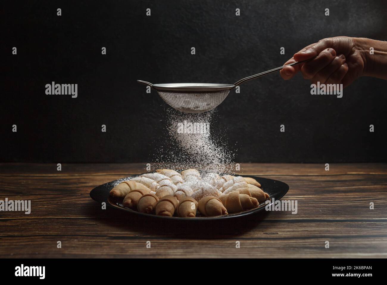 Womens hands sprinkle powdered sugar through a sieve on freshly baked ...