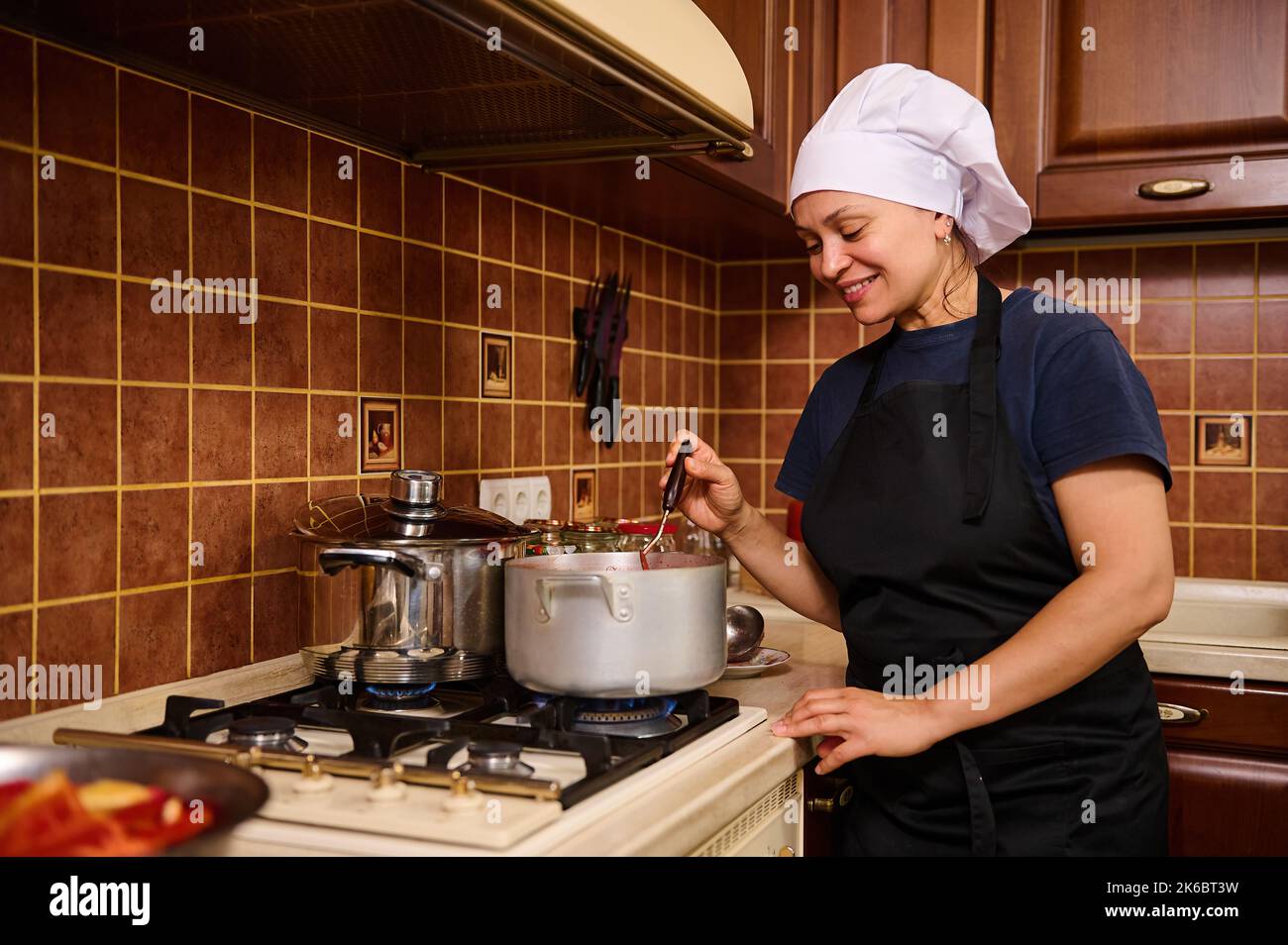 Beautiful woman stirs boiling tomato juice in a saucepan with a kitchen ...
