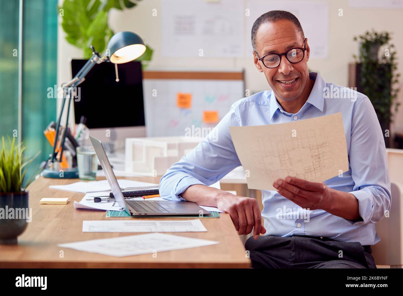 Mature Male Architect Working In Office At Desk Studying Plans For New ...