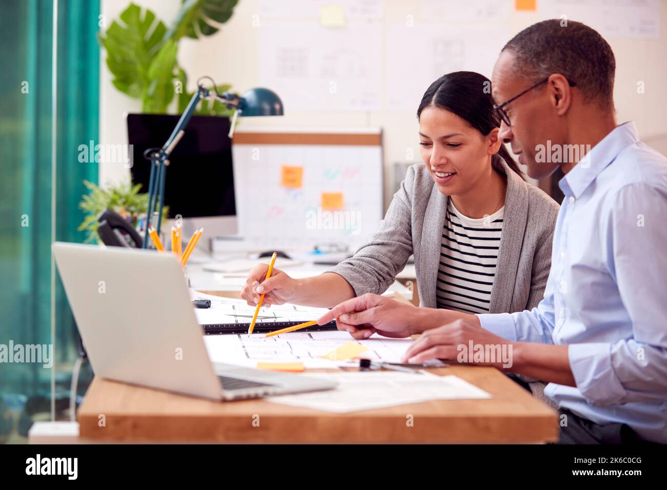 Male And Female Architects Working Together In Office At Desks On Plans ...
