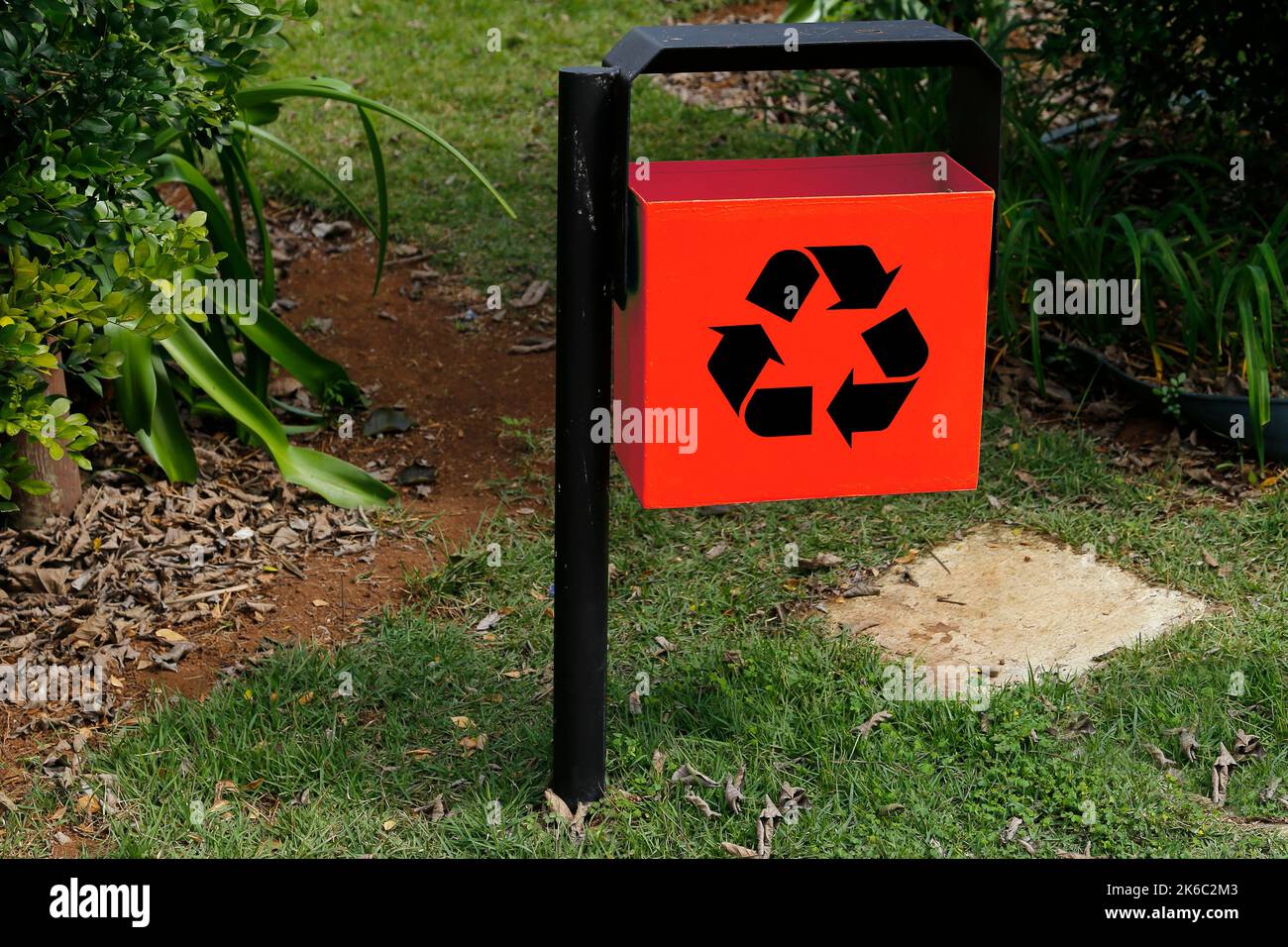 red metal trash can with recycling symbol in green public area and ...