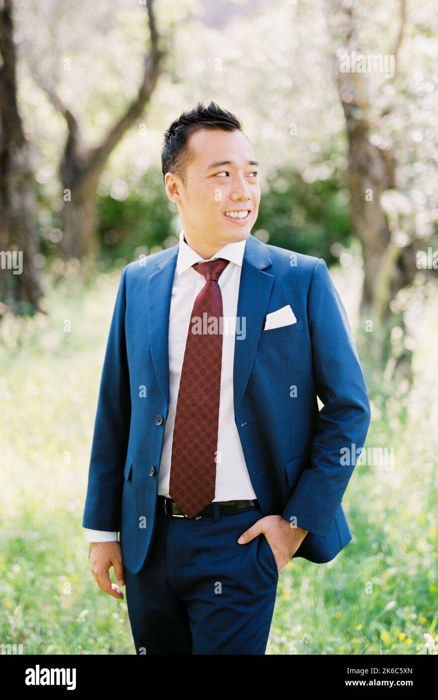 Man in a suit stands under a tree with his head turned to the side ...