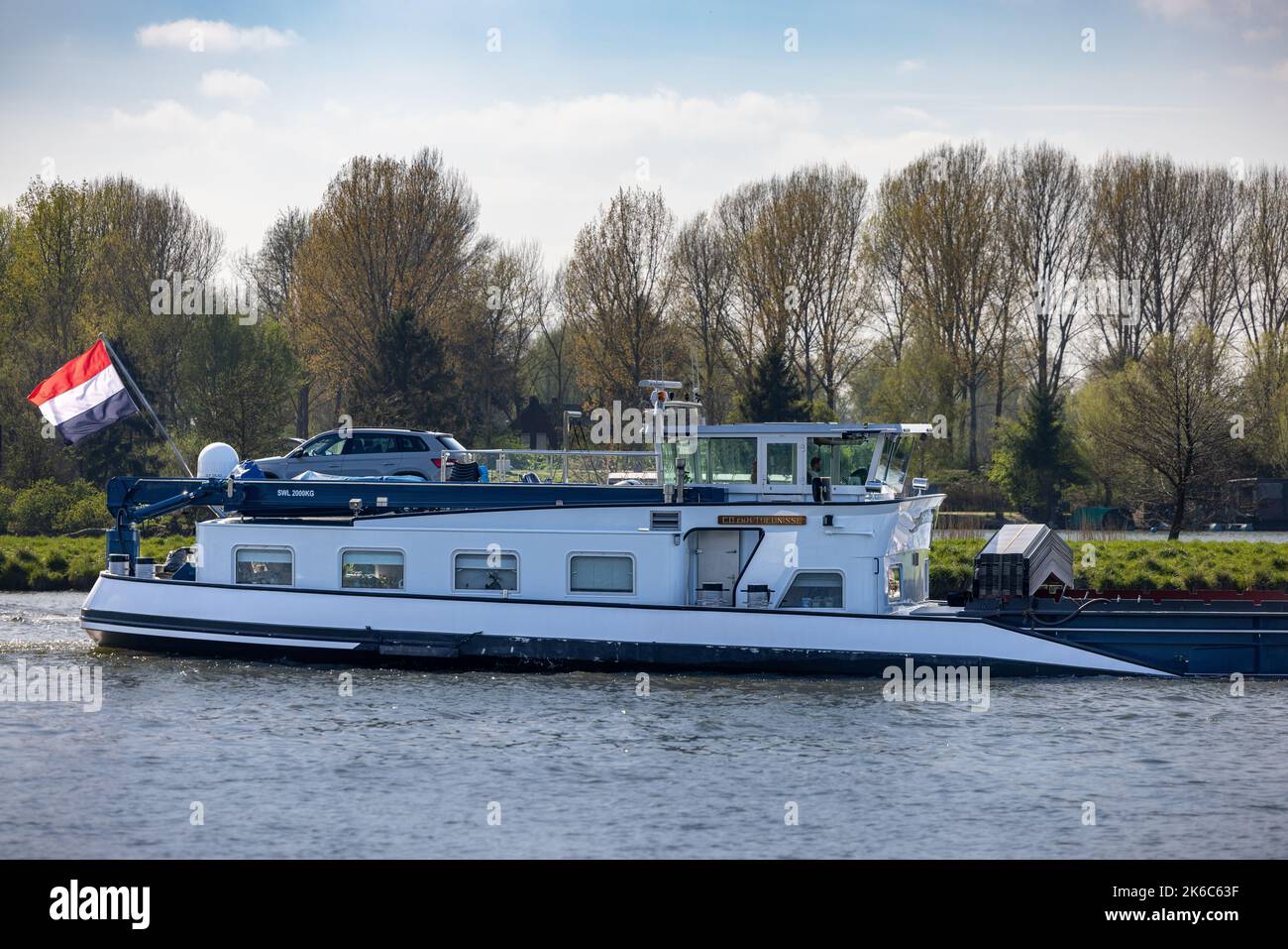 A cargo boat with a Dutch flag on the river Maas in Roermond on a sunny ...